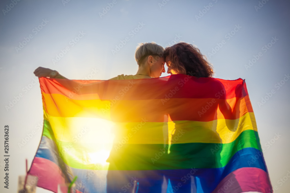 Beautiful lesbian young couple gently lovingly hugging with rainbow ...