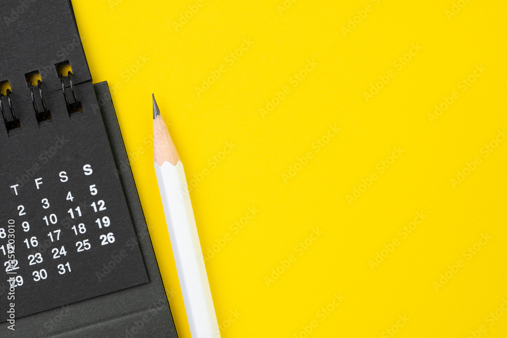 Black clean calendar with white pencil on solid yellow background with ...