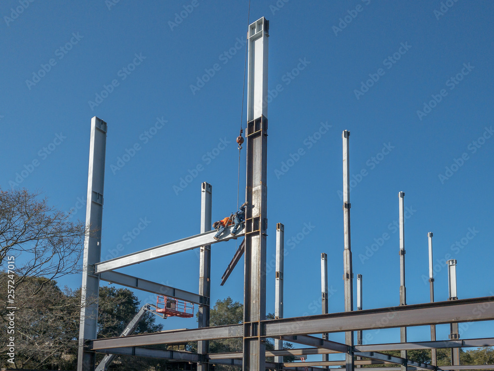 2 ironworkers is straddle a horizontal steel I-beam and reach out to ...