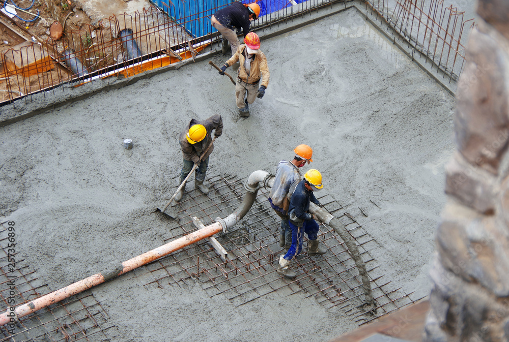 Five workers poured cement construction. Two of them hold a pipe from ...