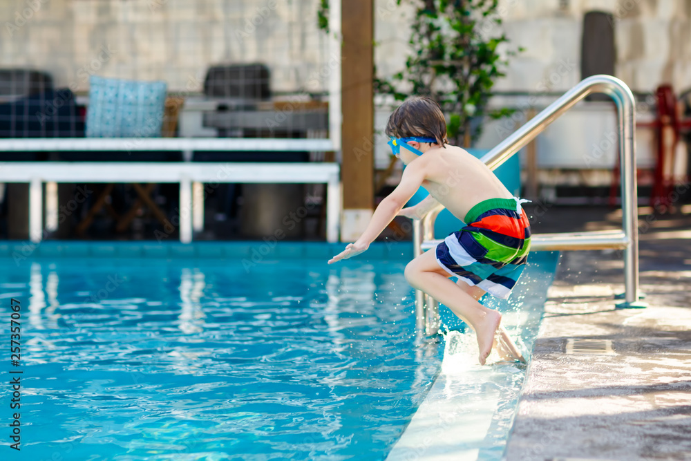 Happy little preschool kid boy jumping into water at pool. Child having ...