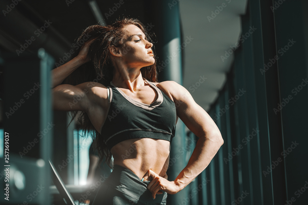 Portrait of beautiful Caucasian female bodybuilder posing in gym with ...