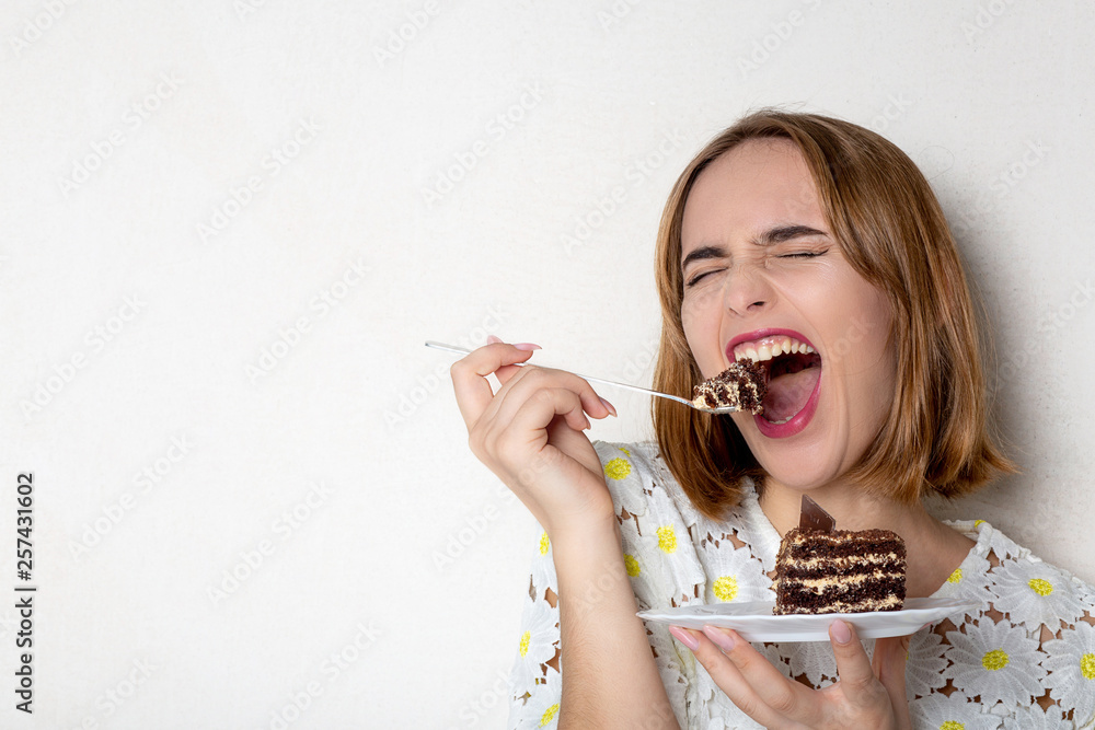 Funny young girl eating tasty chocolate cake over white background ...