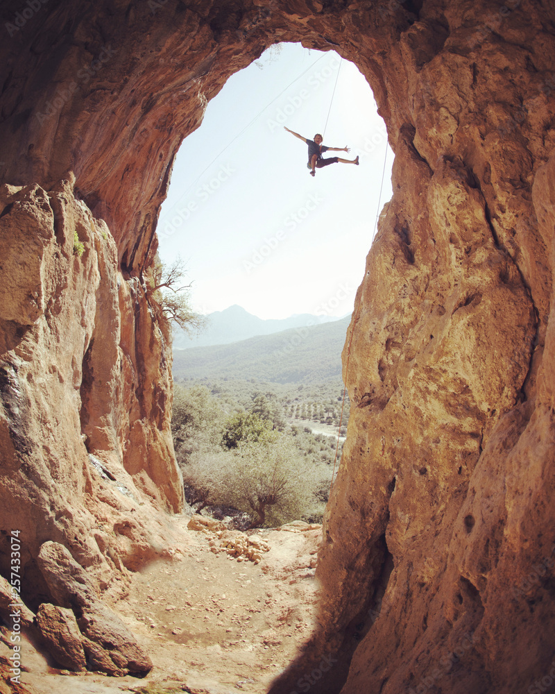 Male rock climber hanging with one hand on challenging route on cliff ...