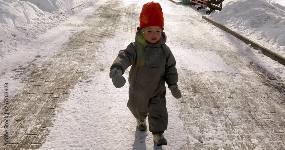 Winter walk with child park. Child gray overalls walks wide road shows ...