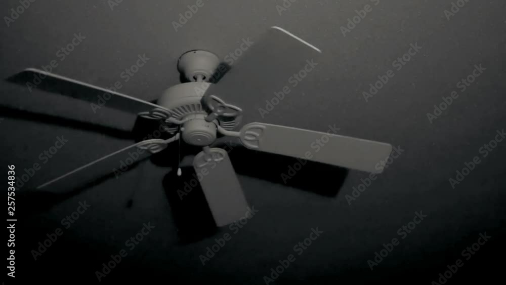 Ceiling fan begins rotating in dark room at night with shadows cast by ...