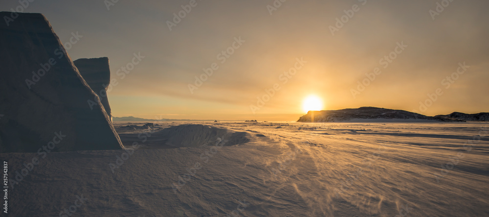 Sunset behind an iceberg looking north across the frozen surface of the ...