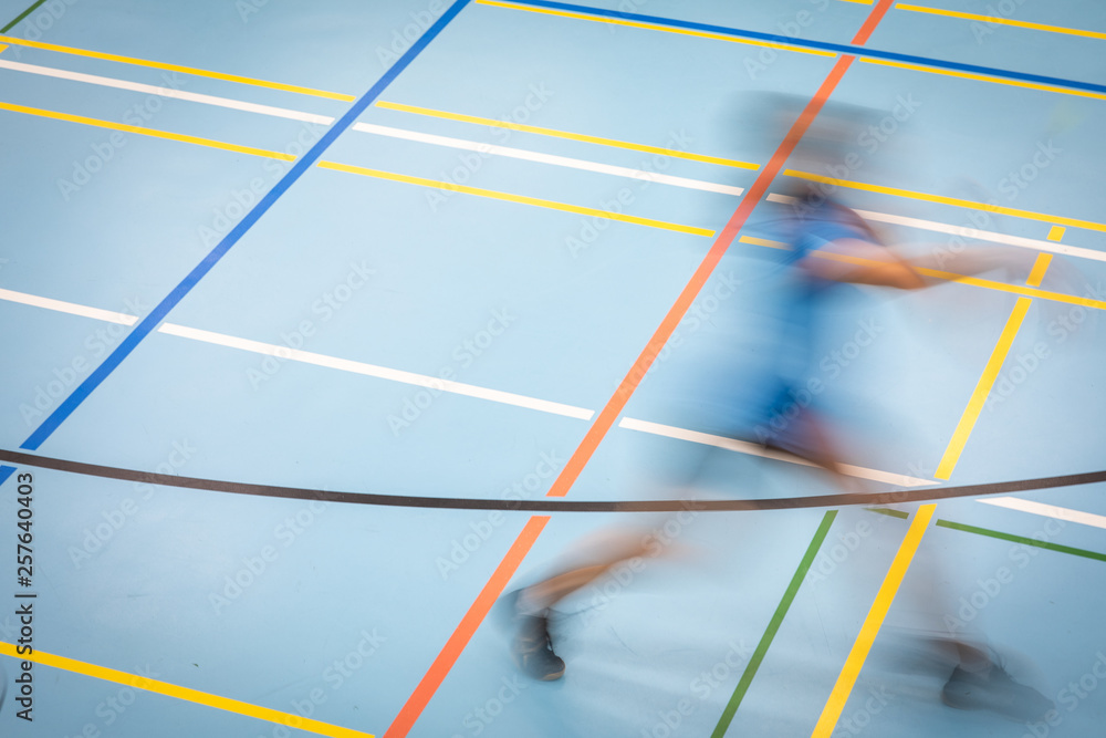 Badminton player in fast motion on a badminton court in a gymnasium ...