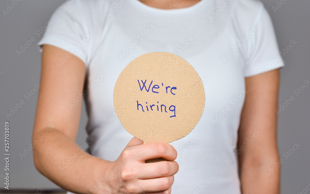 Young women showing round cardboard paper with handwritten text - We're ...