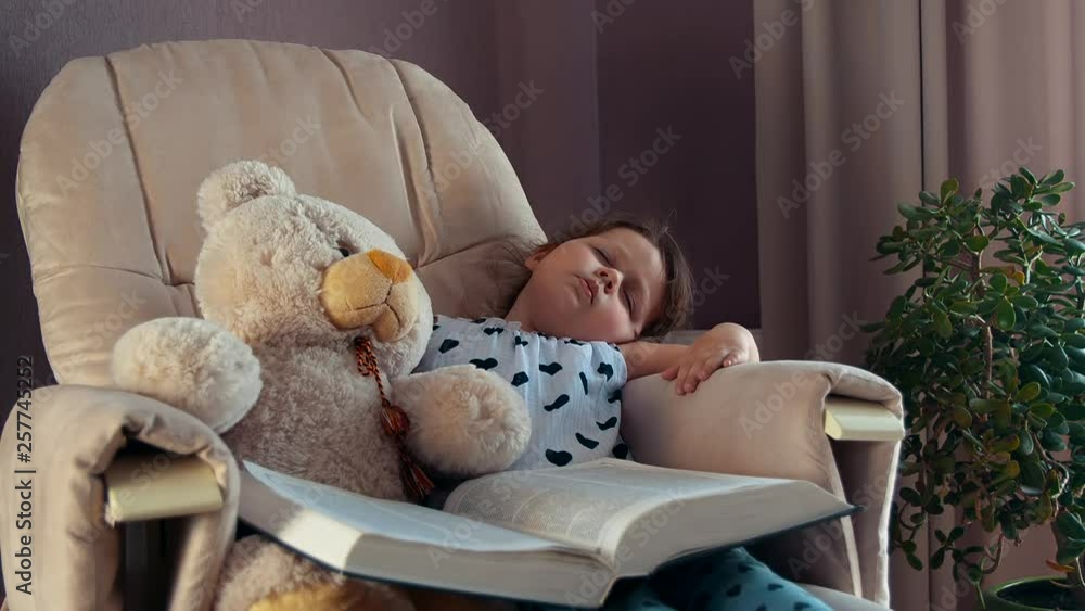 Little girl sleeping on the chair with big book hugging toy teddy bear ...
