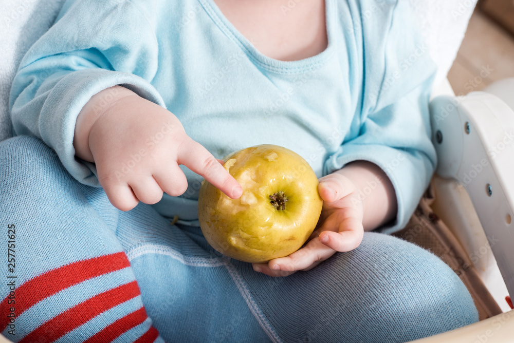 Baby eating fruit. Little boy biting apple sitting in white high chair ...