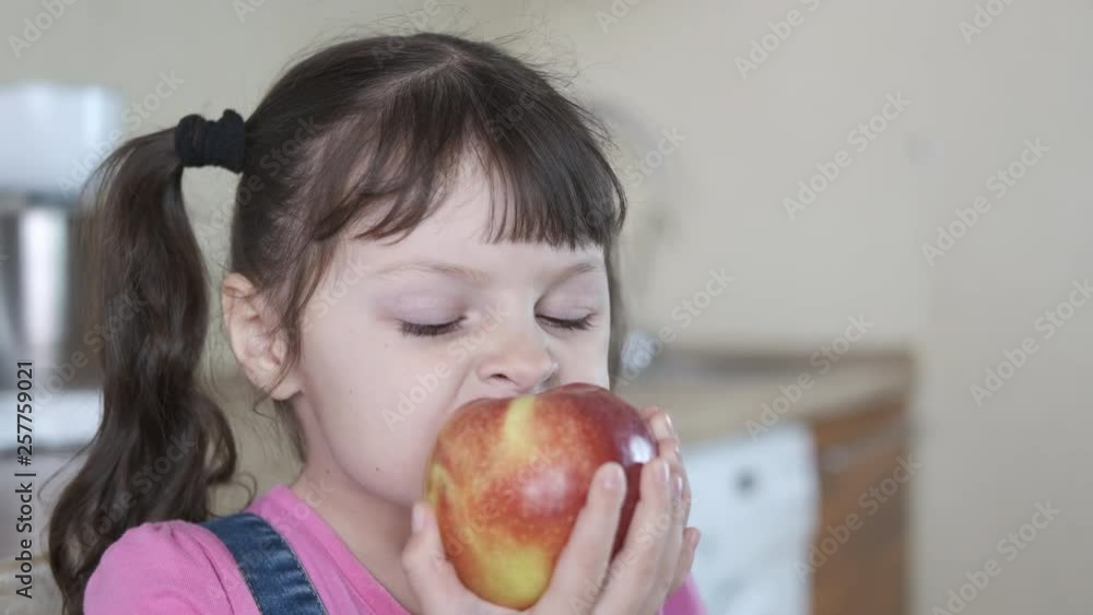 A child in the kitchen is eating an apple. Beautiful little girl eats a ...