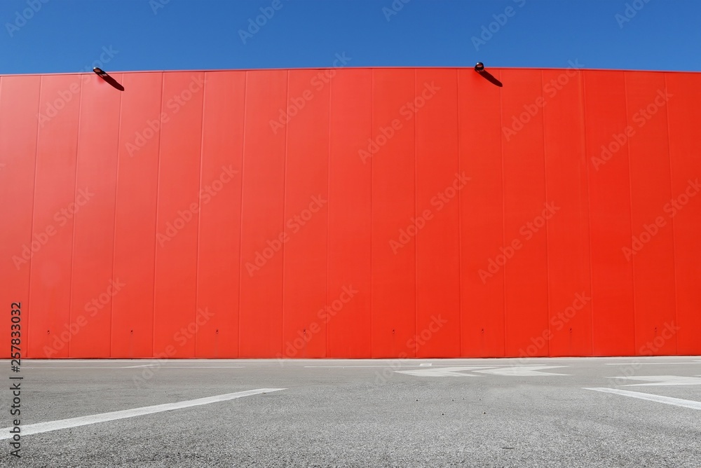 Bright red aluminium cladding wall with an asphalt road in front ...