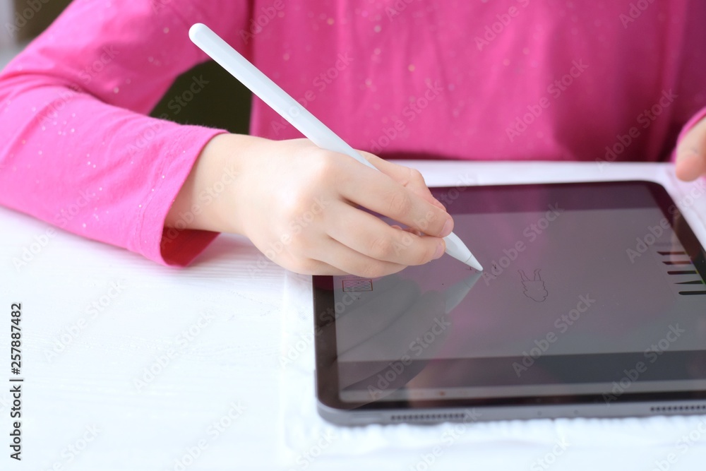 White child hand drawing on tablet screen with white pencil. The girl ...