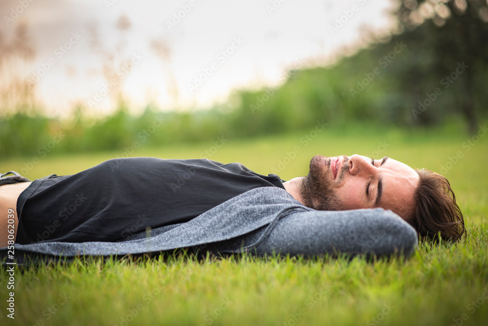 Young teenage man sleeping in the park, lying down in the grass ...