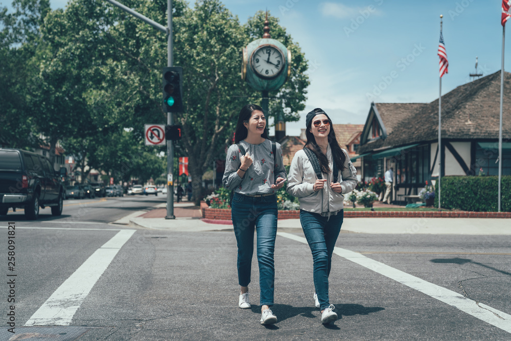 full length two Asian girl friends walking down alley together crossing ...