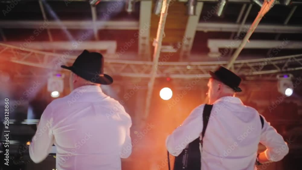 Rear view of a two man singing to microphone and play accordion on blur ...