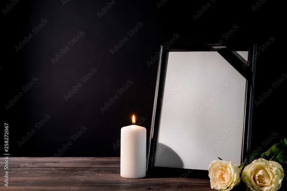 Blank funeral frame, candle and flowers on table against black ...