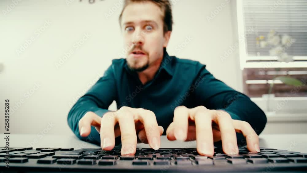 Man doing funny faces while typing on keyboard 4K. Low angle view from behind the keyboard with ...