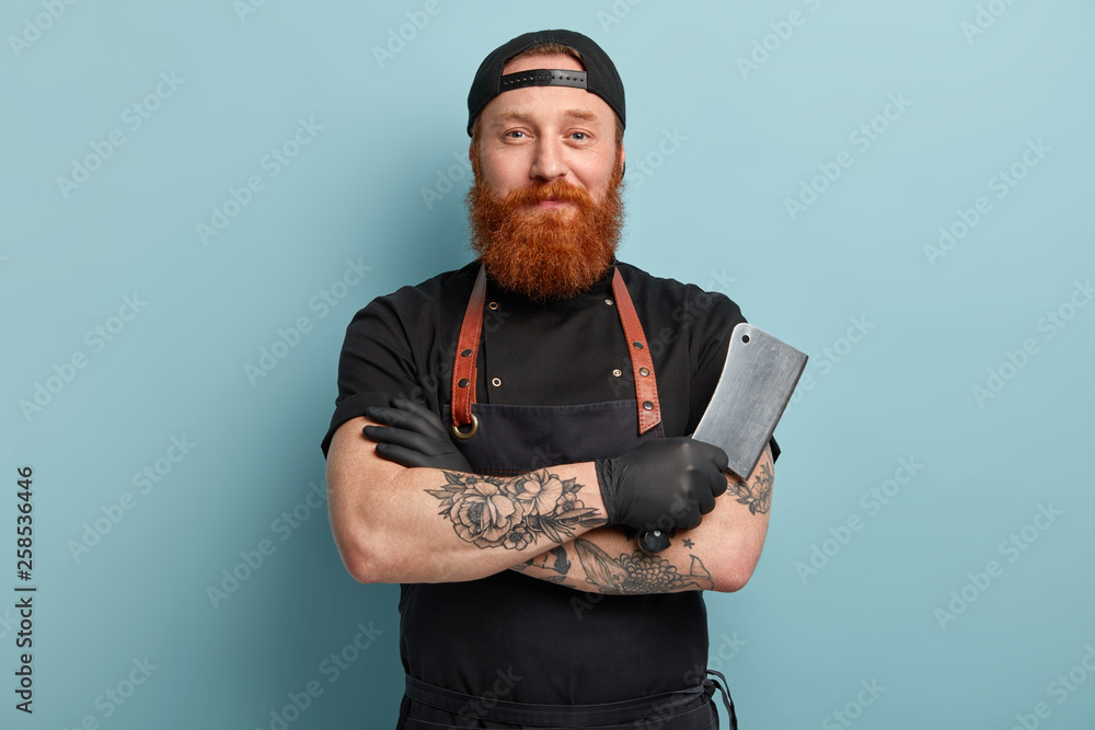 Portrait of handsome professional male butcher has arms crossed, holds ...