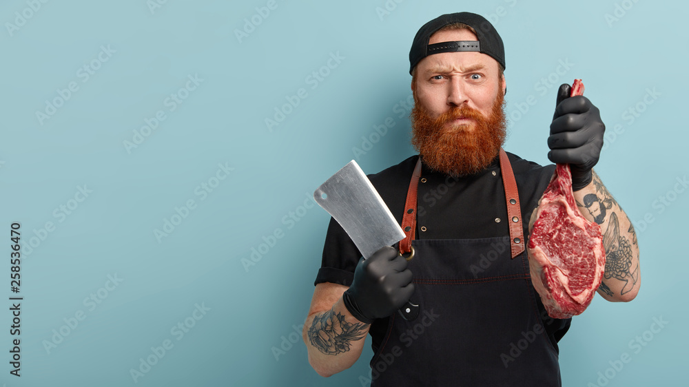 Fotka „Strict serious male butcher holds raw piece of meat, sharp knife ...