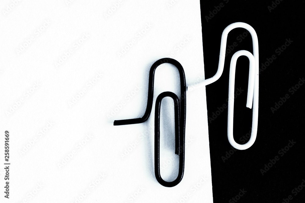 A white-clipped paperclip sits on a black surface and another black ...