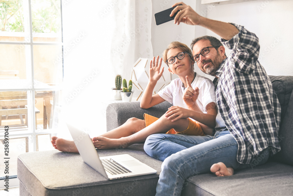 Father and son making a video call sitting on a sofa at home. Wireless ...