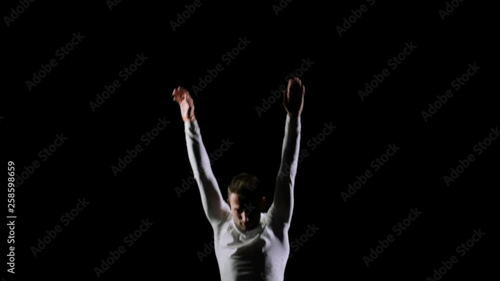 Young handsome male acrobat gymnast in white clothes on a black ...