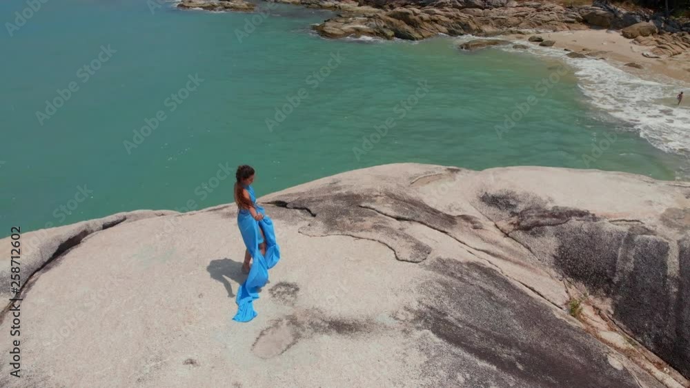 Aerial drone view of beautiful brunette girl in blue long dress dancing ...