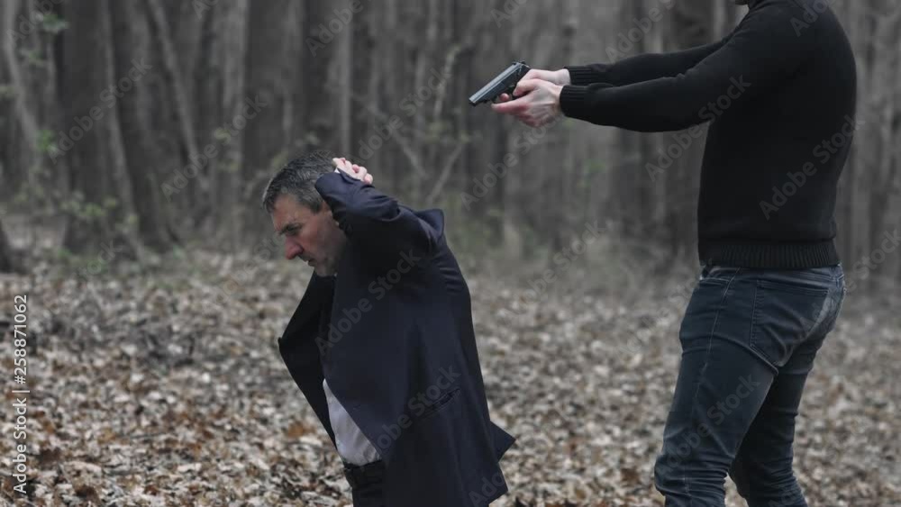 A criminal points the gun to a man's head which knees down on the ...