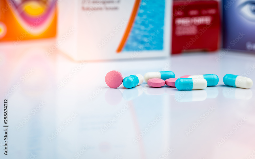 Round pink tablets pill and white-blue capsule pills on blurred ...
