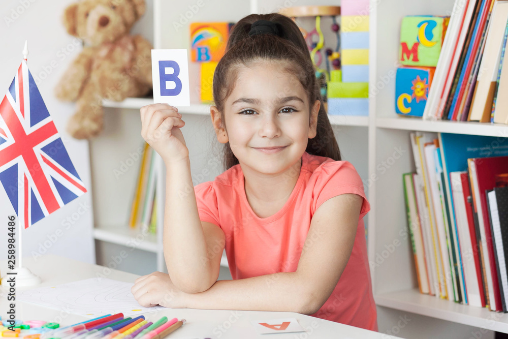 Learning English. Happy cute child girl sitting at a table and draws ...