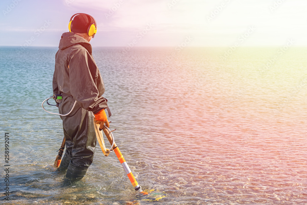 A man standing knee-deep in the water looking for precious metals with ...