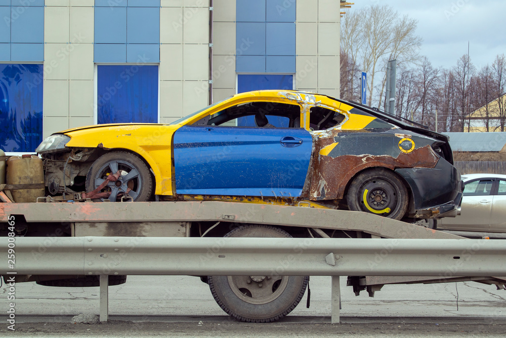 An old, broken, rusty, sports car is on the auto-towing vehicle. The ...