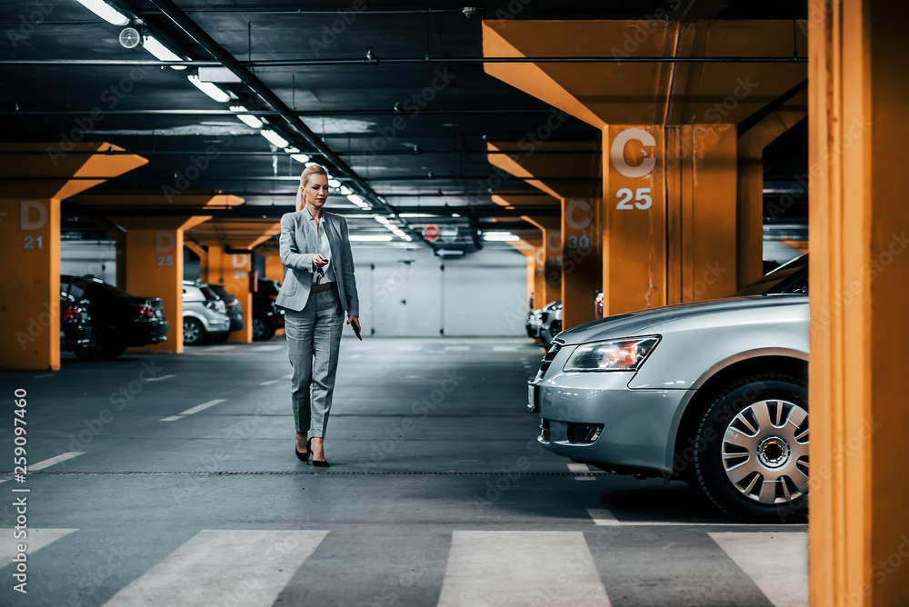 Successful businesswoman walking to her car in underground car parking ...