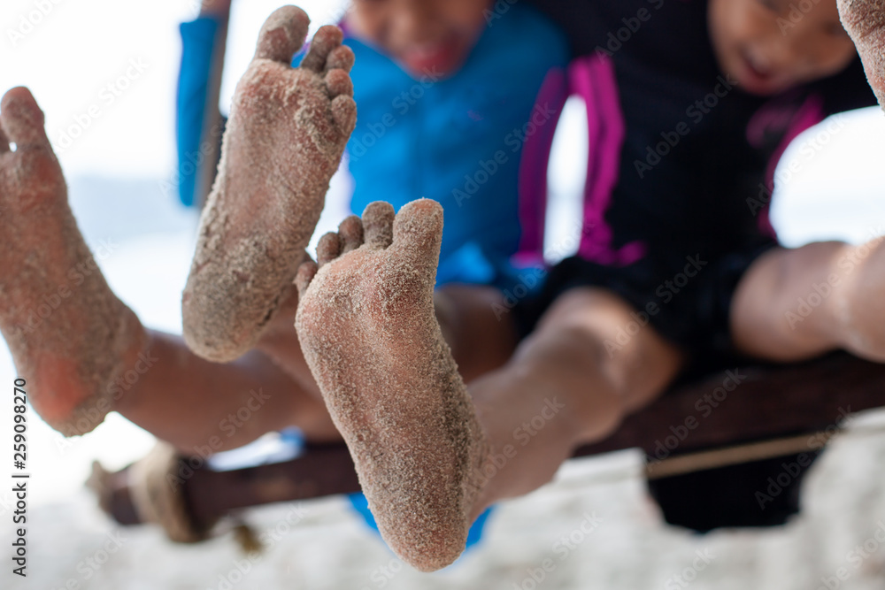 Children bare feet with sand while they playing on a swings together at ...