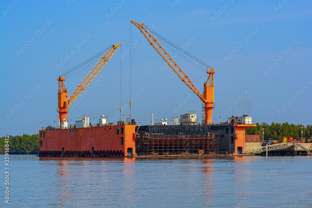 Submersible floating dry dock with dock cranes moored at river bank ...