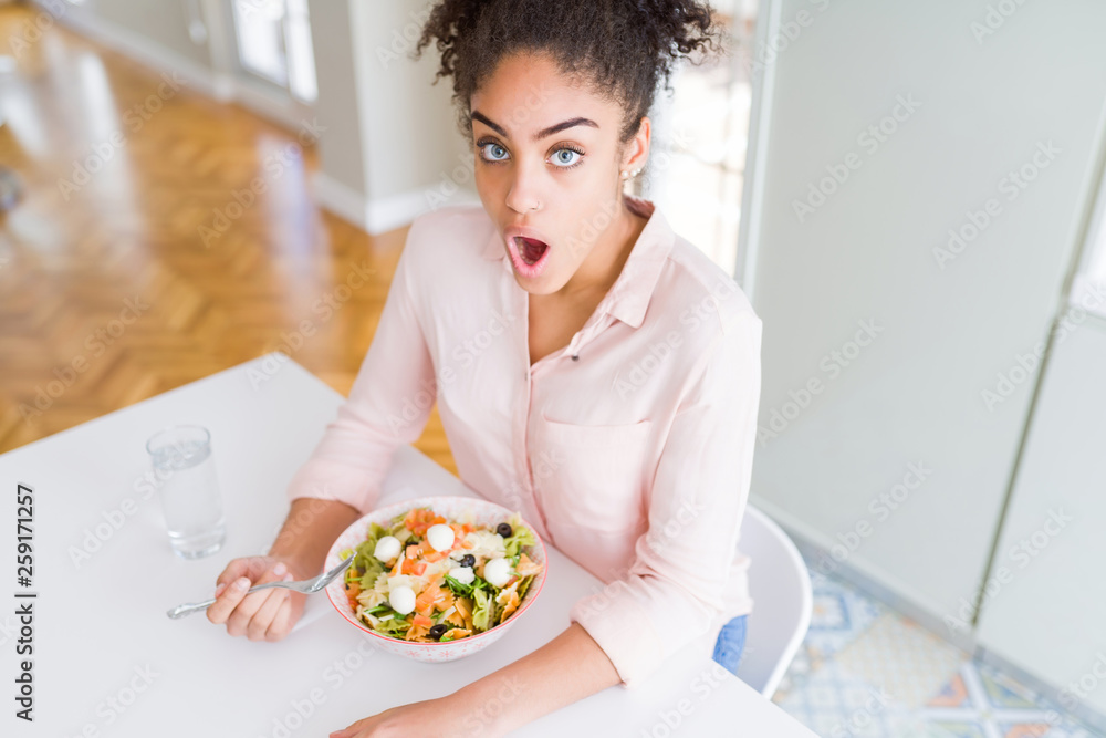 Young african american woman eating healthy pasta salad scared in shock ...