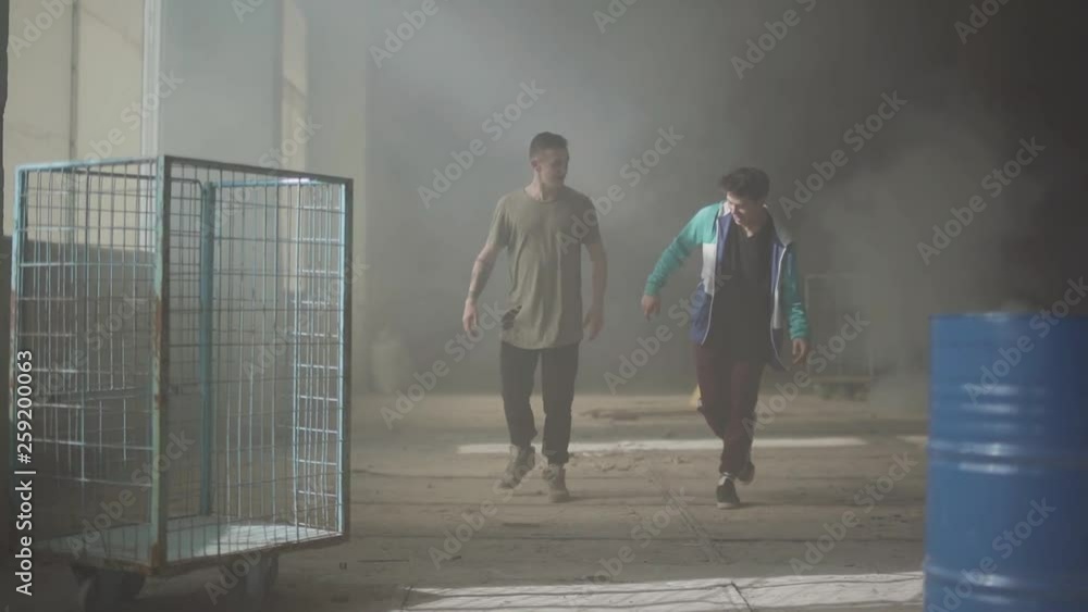 Two young men dancing in the dark and dusty room of abandoned building ...