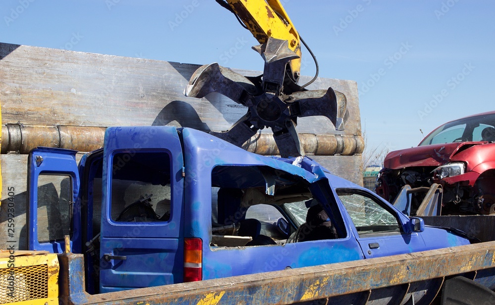 Claw from a crane at junkyard left an old blue car at wrecker press to ...