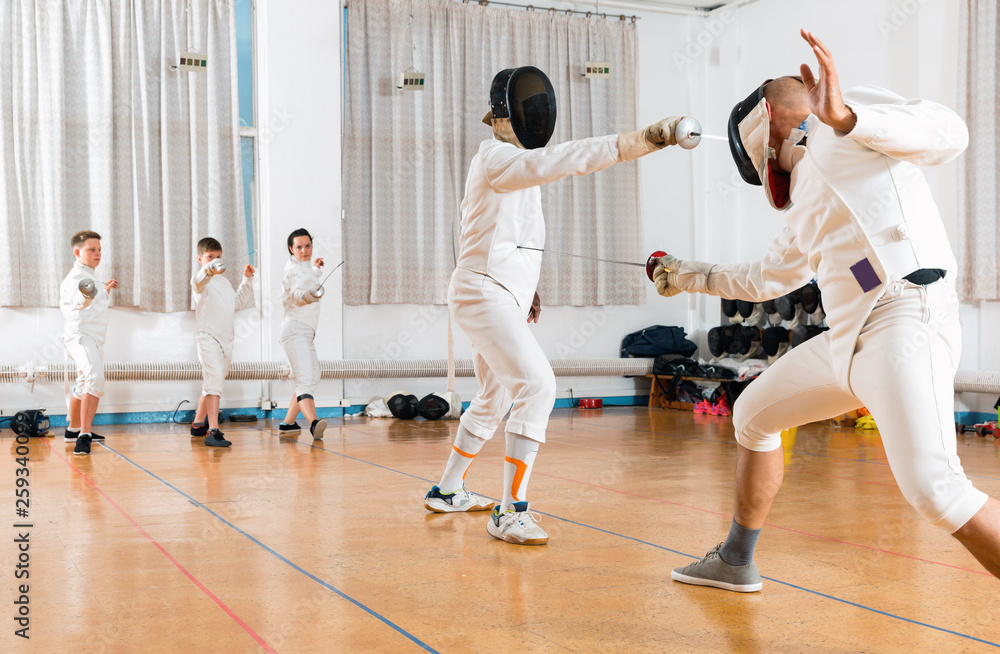 Coaches demonstrating to young athletes attack movements with rapier ...