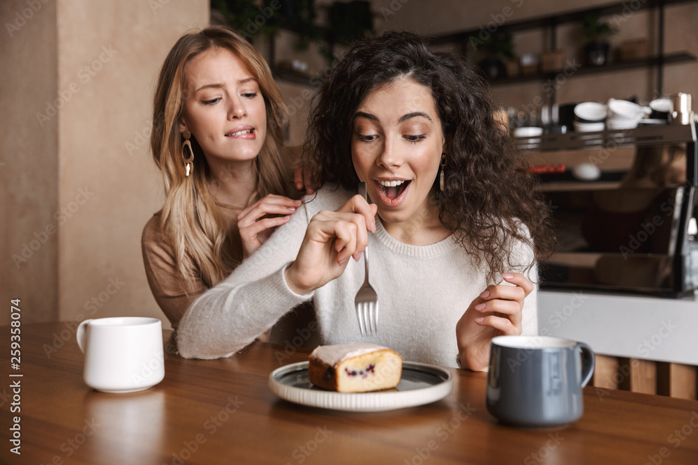 Excited happy pretty girls friends sitting in cafe drinking coffee eat ...