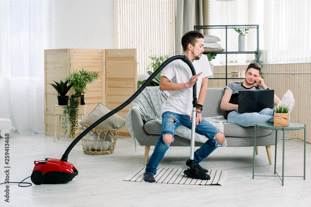 Happy gay man cleaning home, dancing with vacuum cleaner and having fun ...