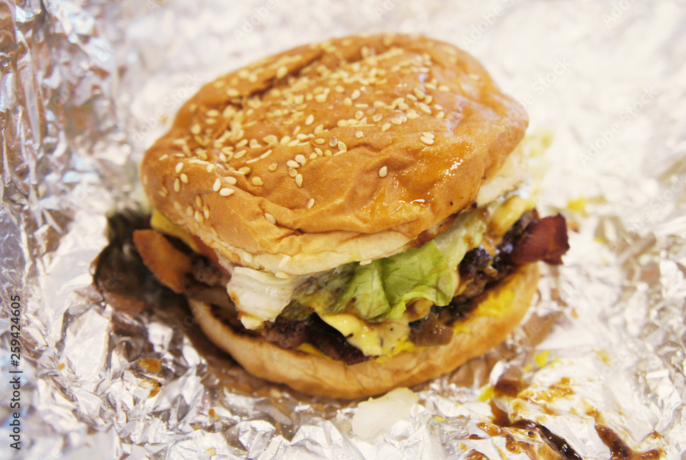 Bad-looking fast food hamburger on a silver wrapping paper. Ugly food ...