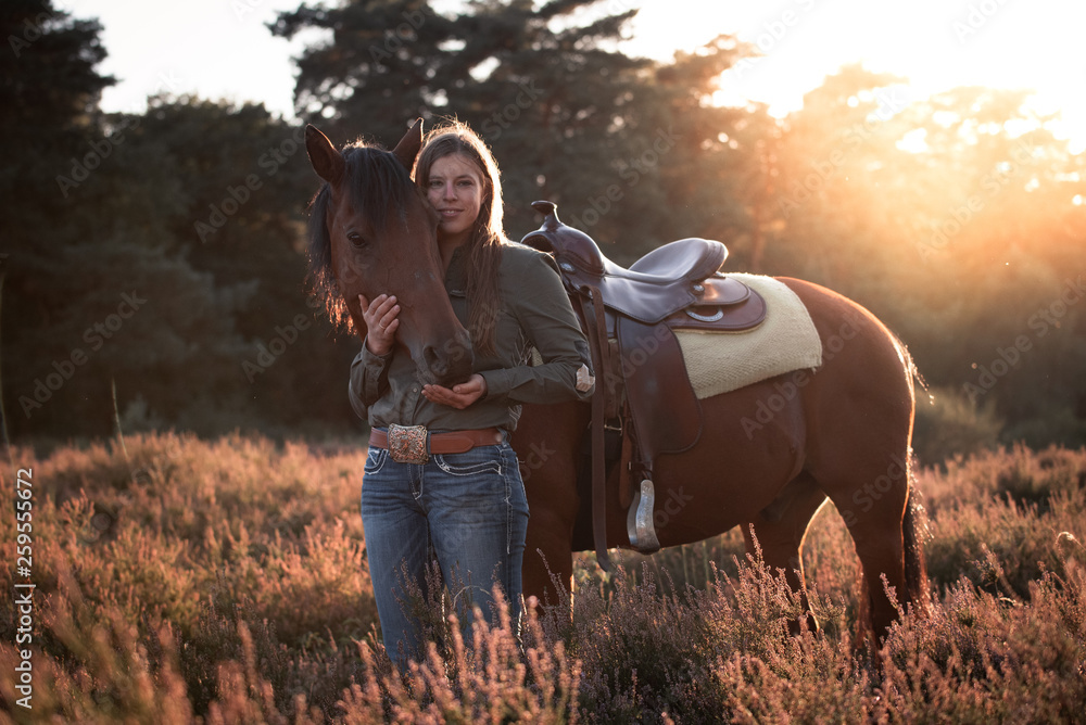 Reiterin steht mit ihrem Quarter Horse im Sonnenuntergang in der Heide ...