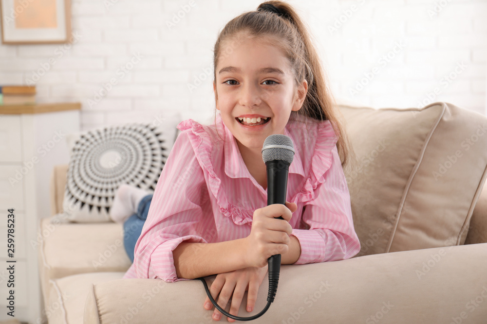 Cute girl with microphone on sofa in living room Stock Photo | Adobe Stock
