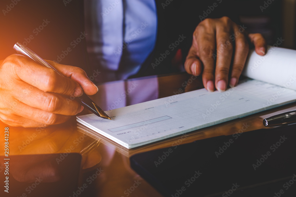 Business woman hand writing cheque bookwith laptop computer and mobile ...