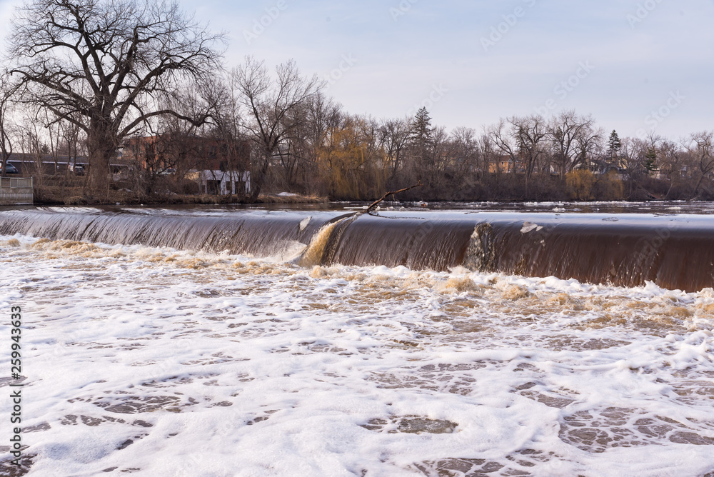 Fast moving river water flowing over concrete dam. Ice floes and chunks ...