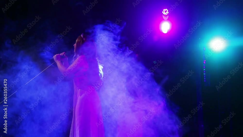 A young red-haired singer sings on stage with professional lighting and ...
