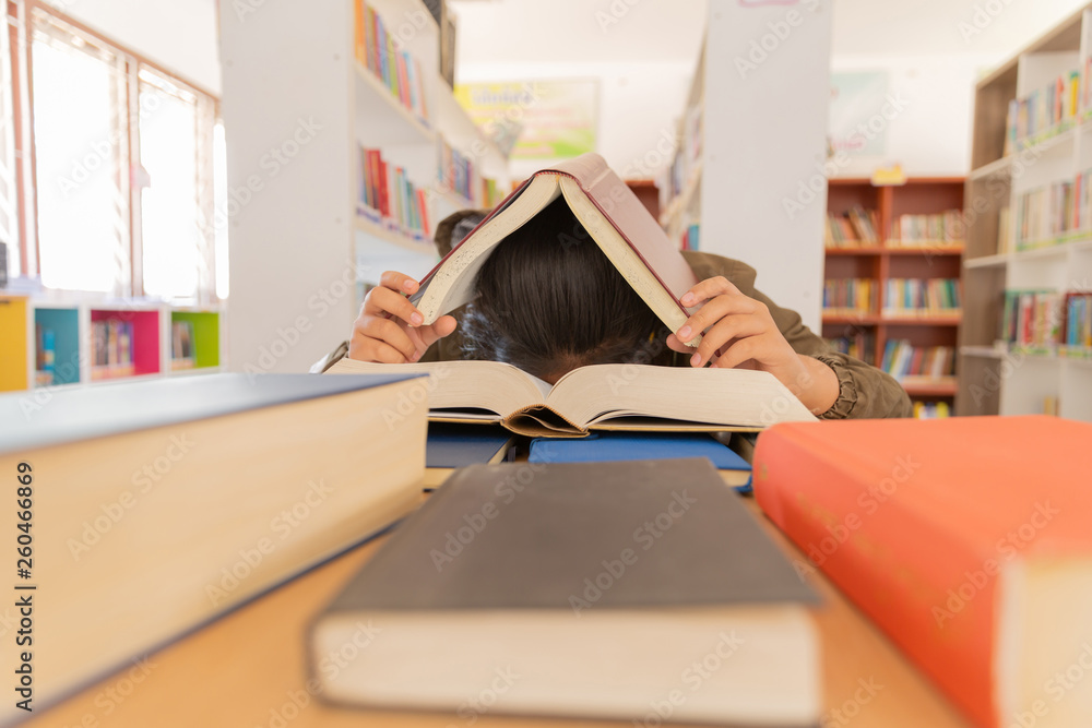 Confused female student laying between stacks of books, looking up with ...